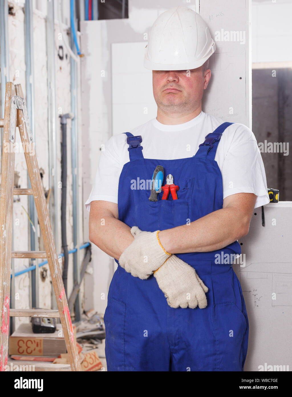 Portrait of tired male builder leaning on wall in repairable room Stock ...