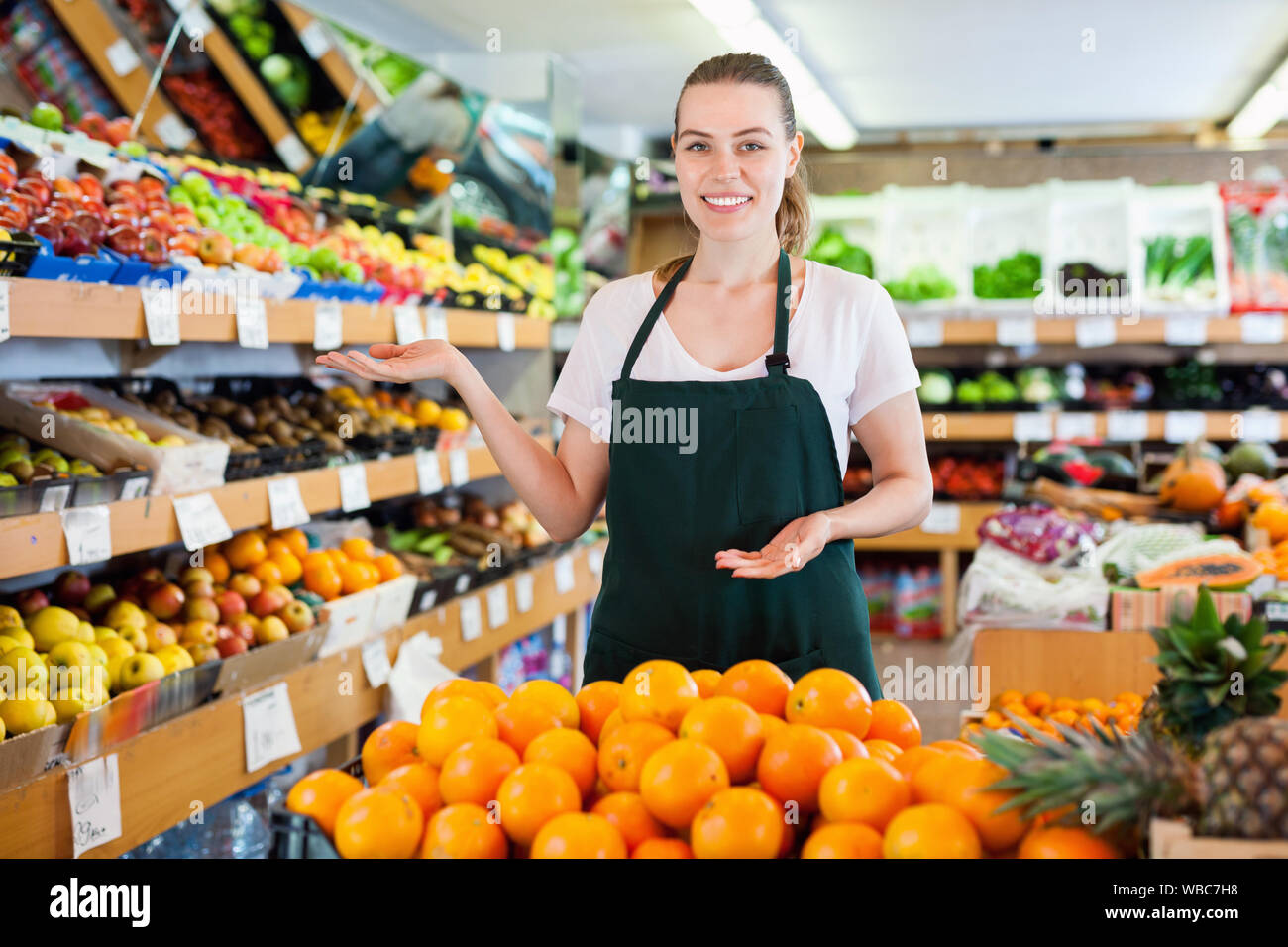Young happy cheerful positive female seller standing and welcoming on ...