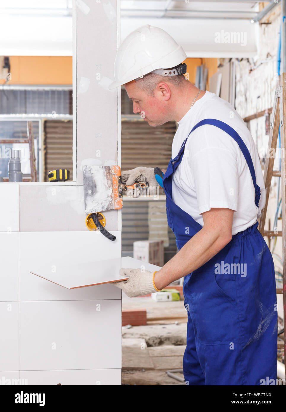 Focused construction worker engaged in wall tiling work during ...