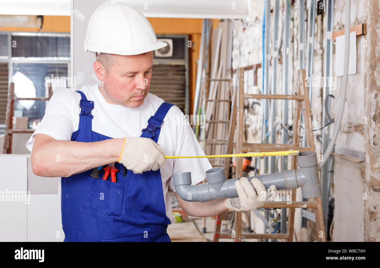 Focused plumber working with metal-reinforced plastic pipes at indoors ...