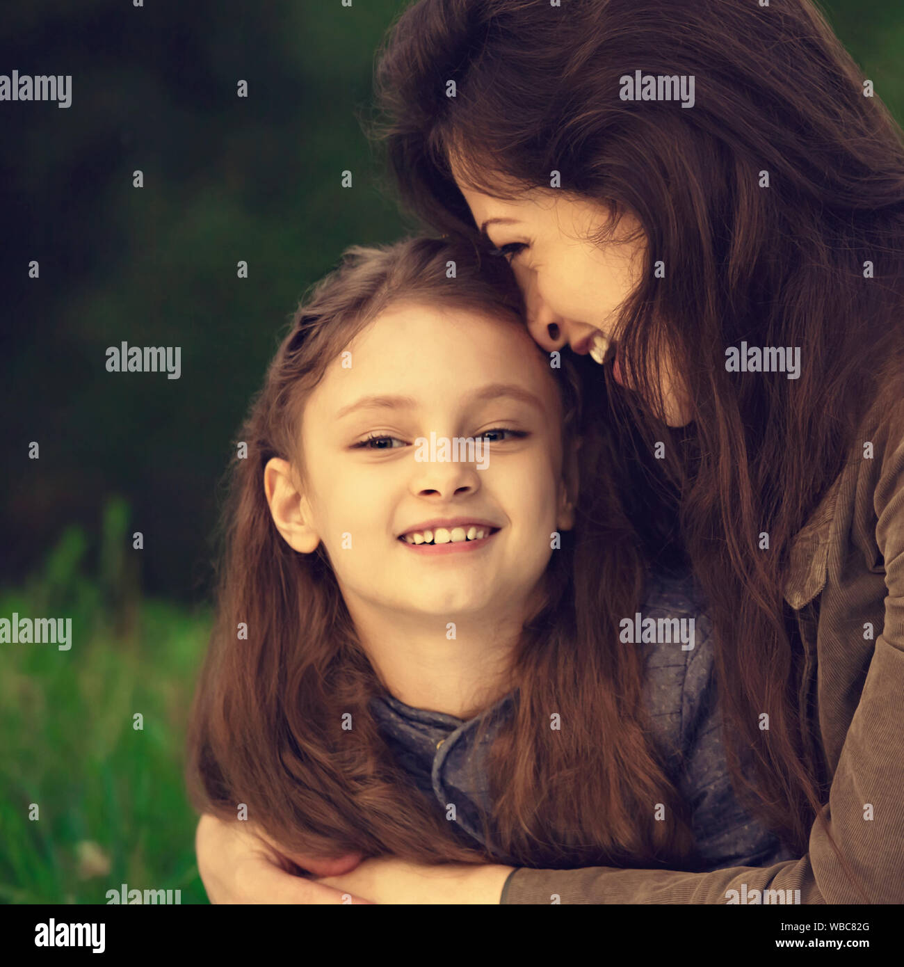 Beautiful young laughing mother embracing her cute long hair daughter ...