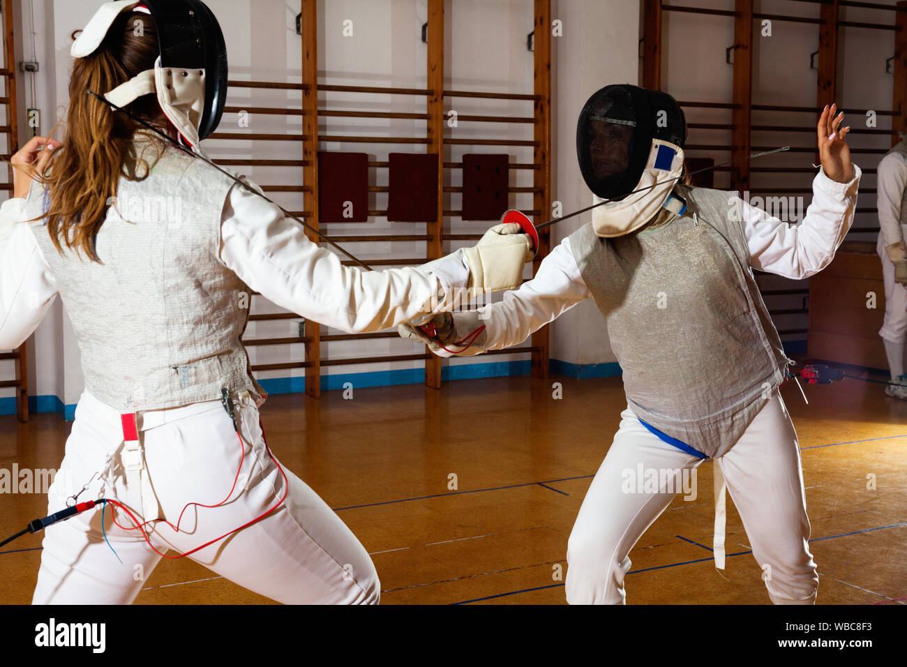 Two glad smiling female fencers exercising movements in duel at fencing ...