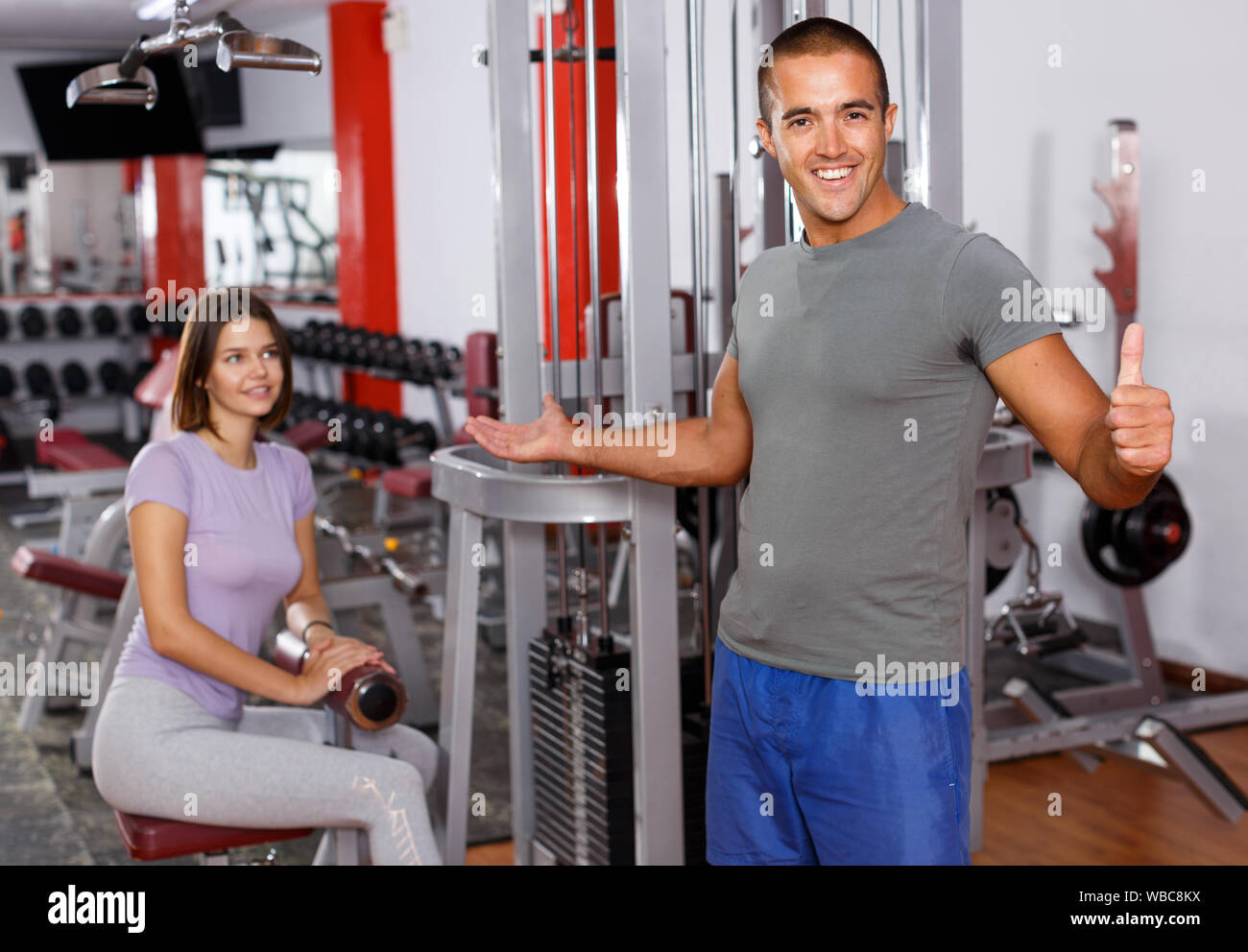 Positive trainer of sports club welcoming with thumb up and young woman ...
