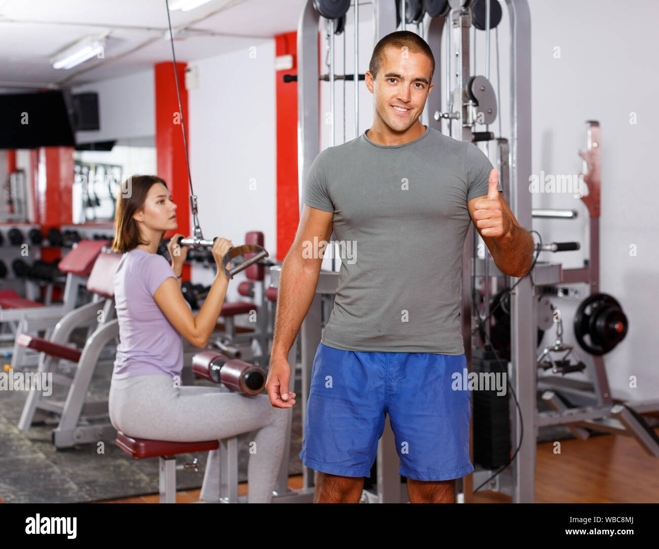 Positive trainer of sports club welcoming with thumb up and young woman ...