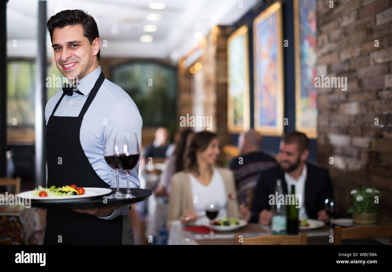 Adult cheerfful waiter standing with tray with glass and salad Stock ...