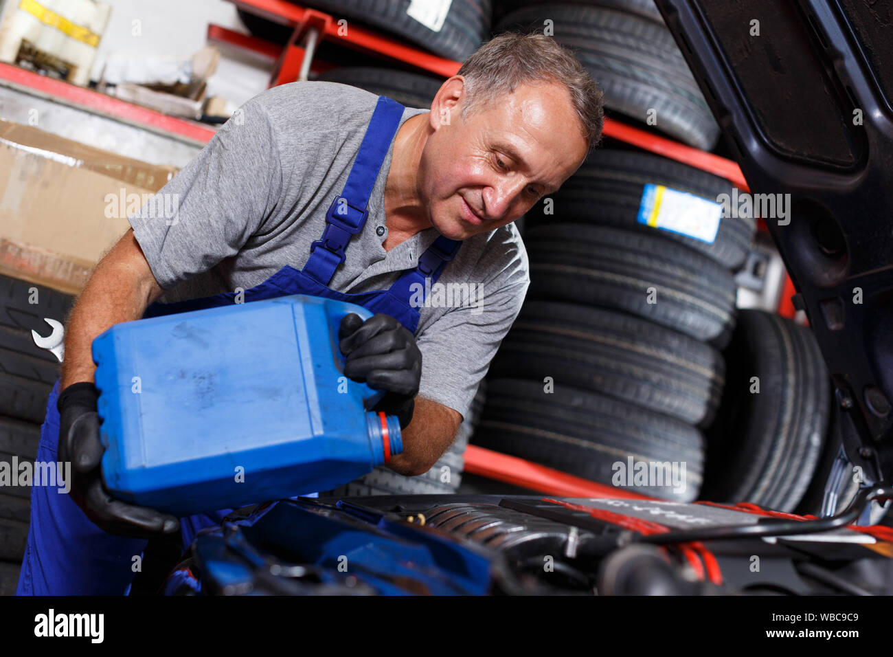 Elderly man mechanic engaged in replacement of engine oil in auto ...