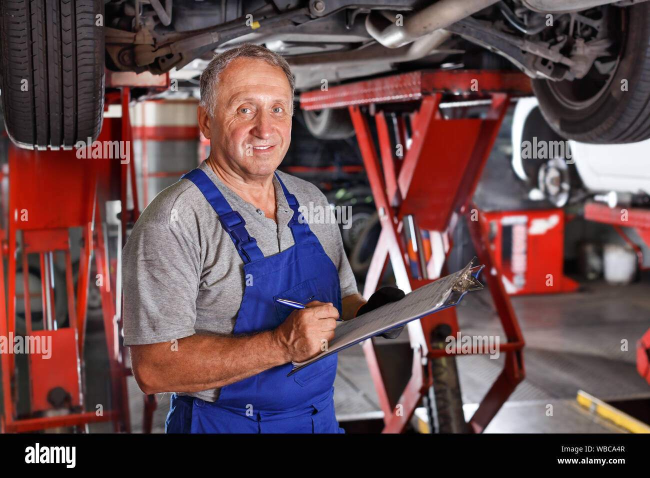 Confident male car mechanic in workshop writing job sheet for repairs ...