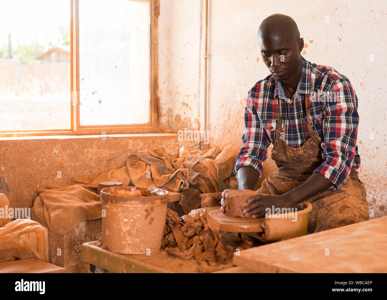 Concentrated African craftsman enjoying work with clay on potter wheel ...