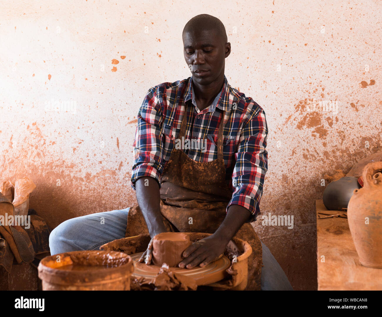 Concentrated African craftsman enjoying work with clay on potter wheel ...