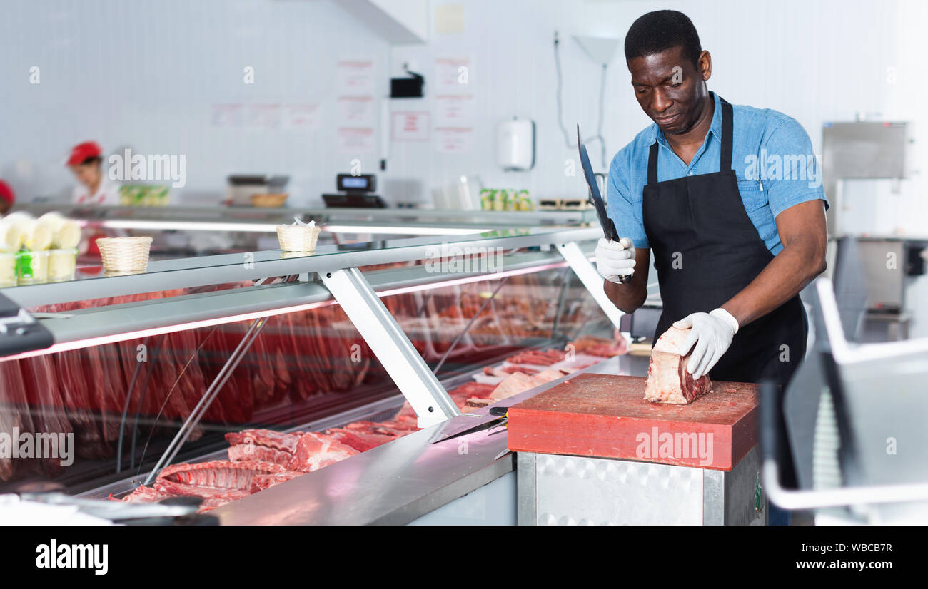Confident glad cheerful positive African American male butcher cutting ...