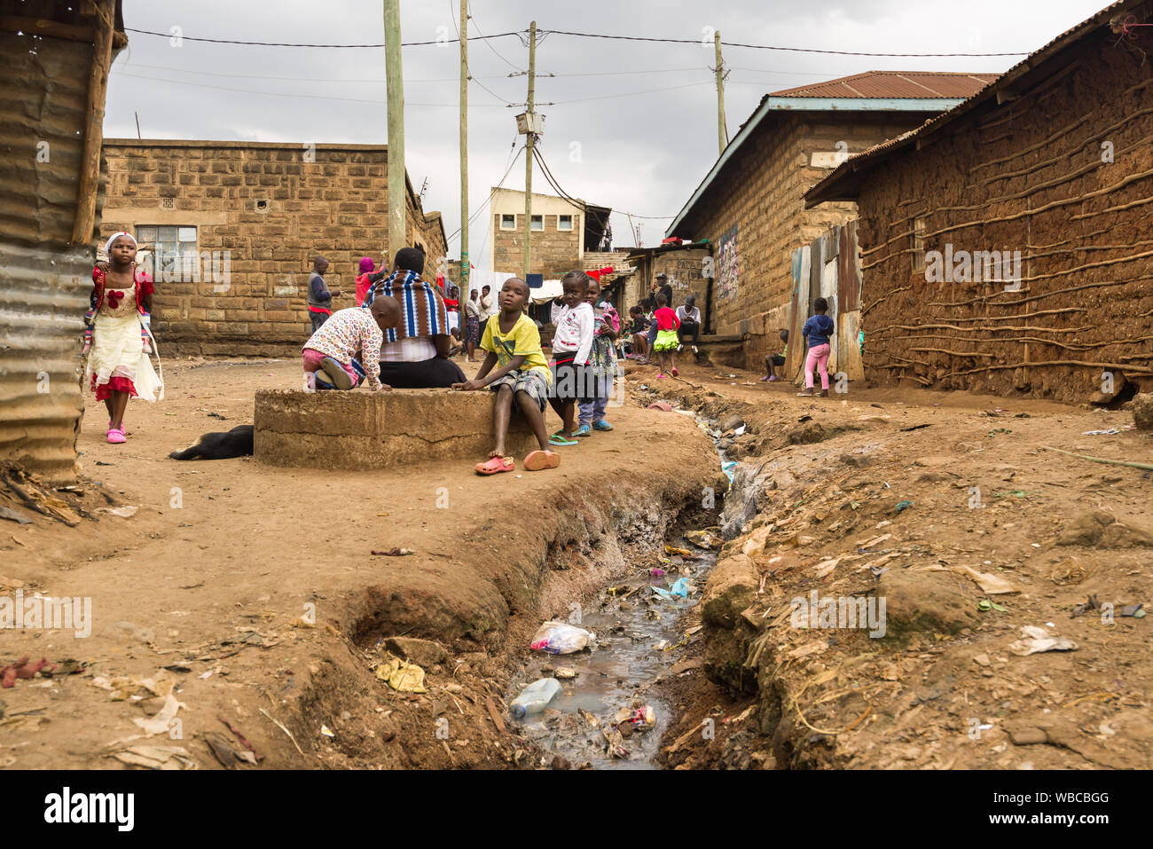 An open sewer flowing between buildings with children and adults beside ...