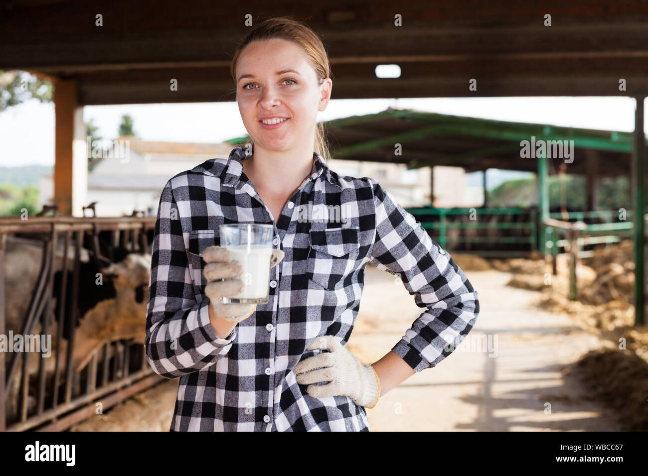Portrait of cheerful female owner of dairy farm with glass of milk in ...