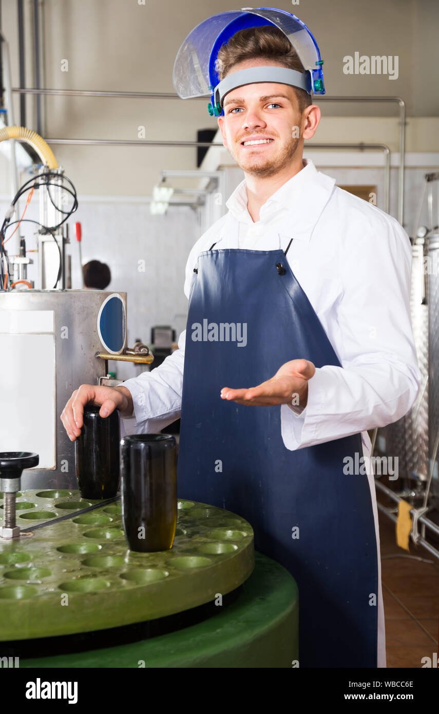 happy adult male employee operating machine at sparkling wine factory ...