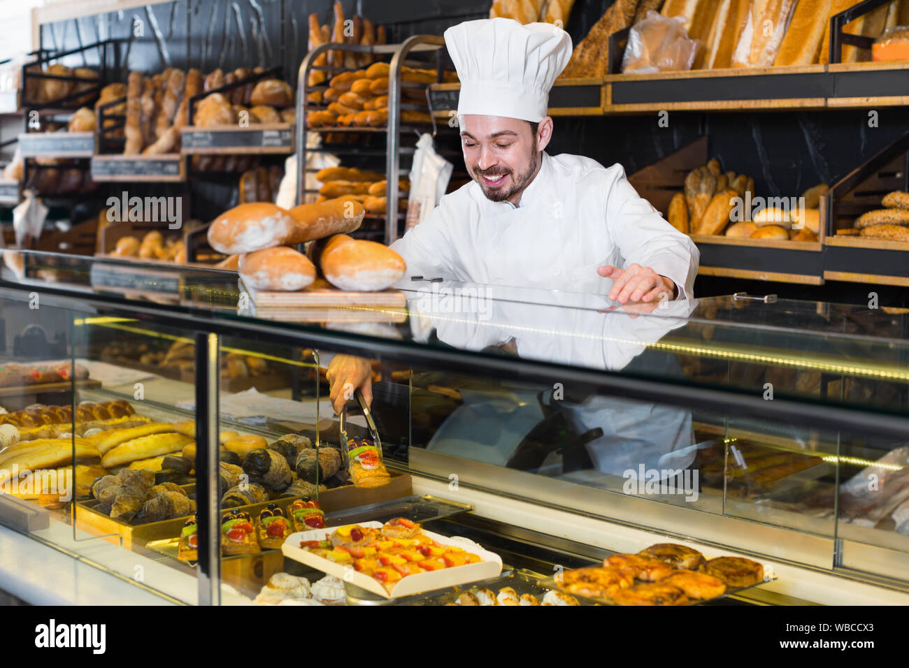 Smiling cheerful positive man seller showing warm festive cake in ...