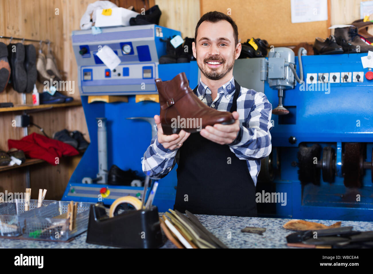 Young smiling friendly male worker demonstrating repaired shoes in shoe ...