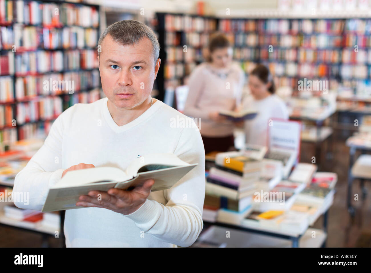 Focused positive man looking for information in books in bookstore ...