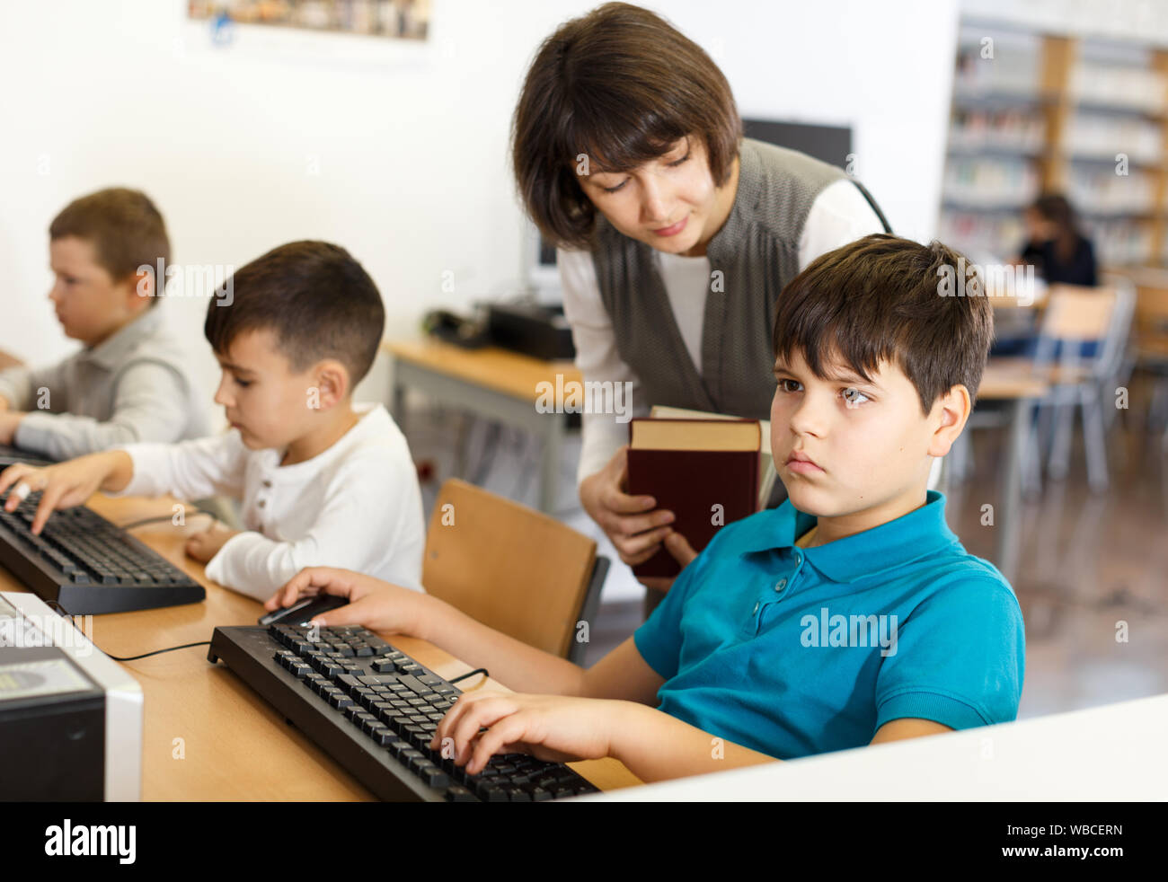 Young female teacher working with pupil in computer class of school ...