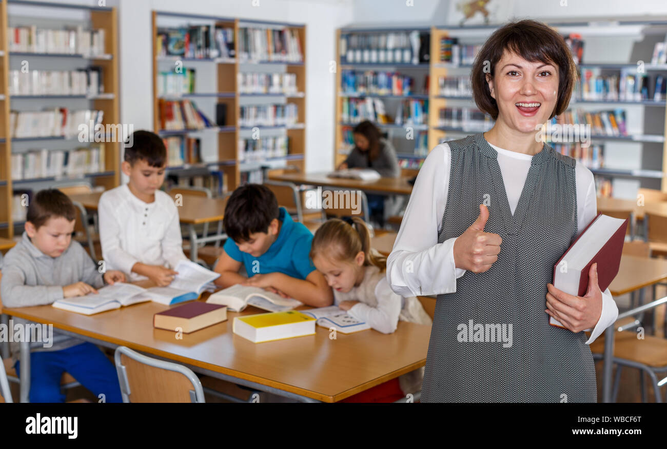 Portrait of happy female librarian standing with book in hands in ...
