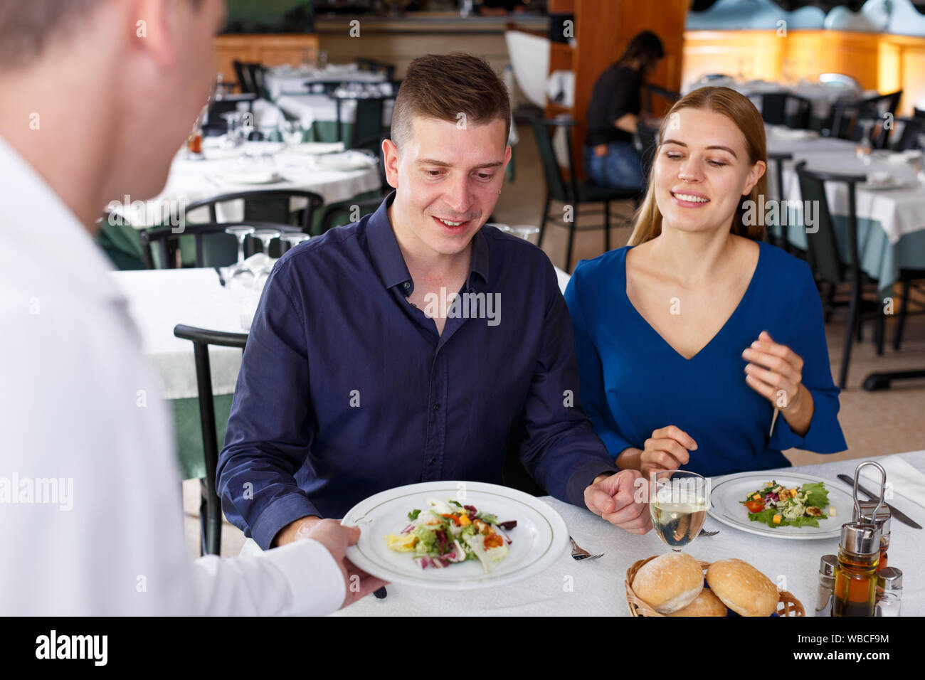 Friendly waiter serving tasty dishes – order of couple having dinner at ...