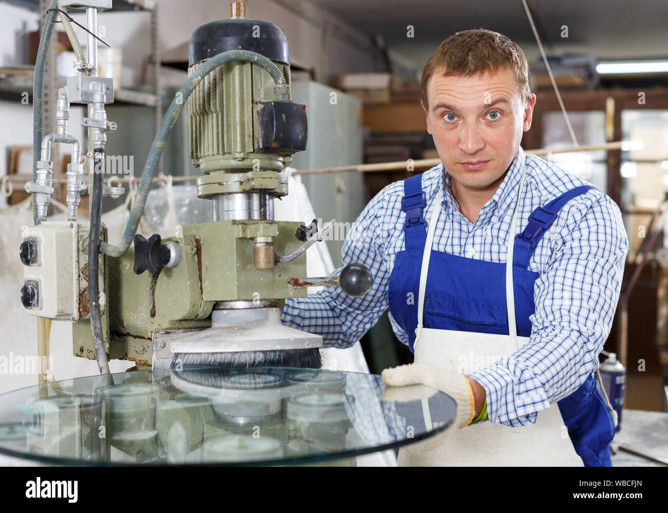 Experienced male worker of glass factory engaged in processing of ...