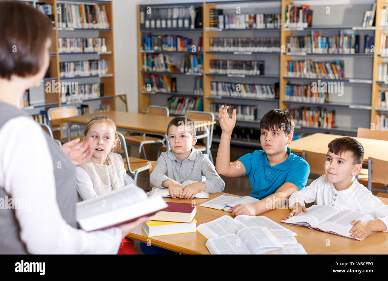Group of school kids studying in school library with friendly female ...