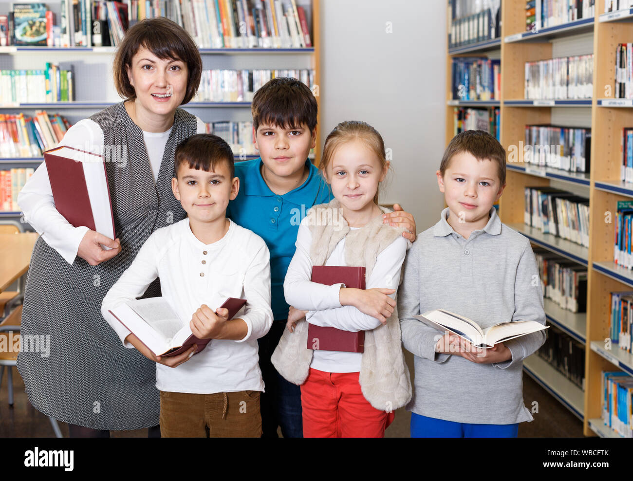 Young female librarian posing together with happy children near ...