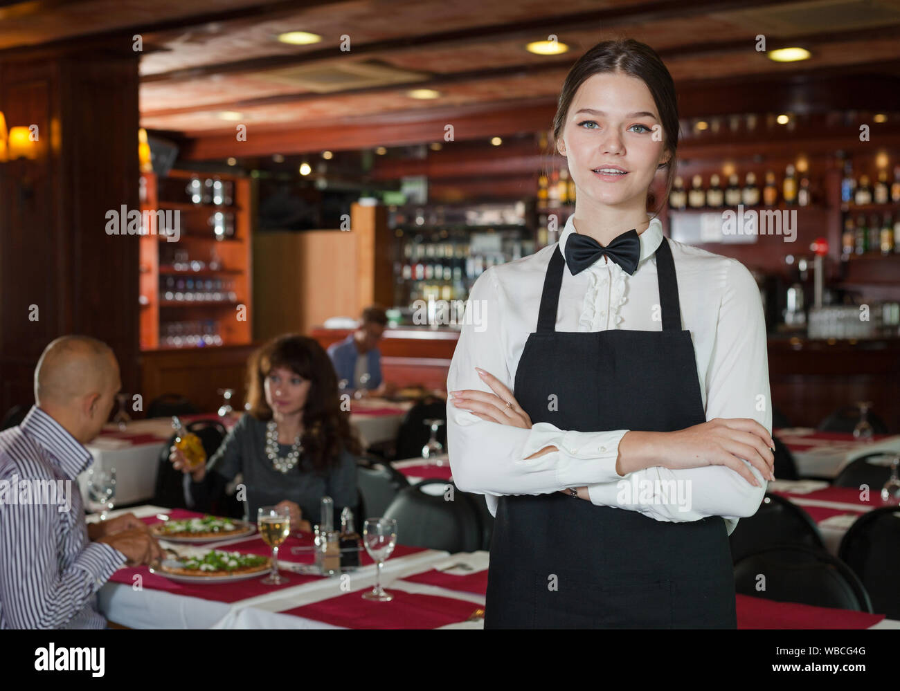 Portrait of polite waitress wearing black apron in restaurant interior ...