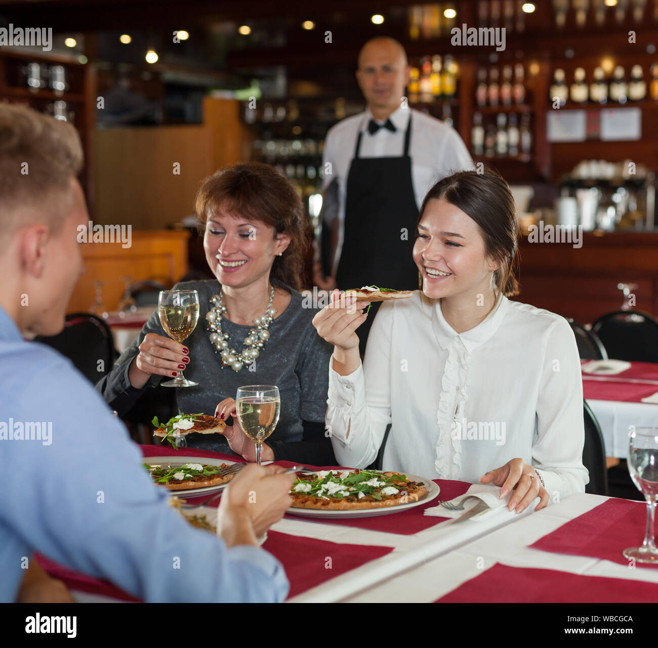 Two attractive girls with male friend enjoying evening meal in cozy ...