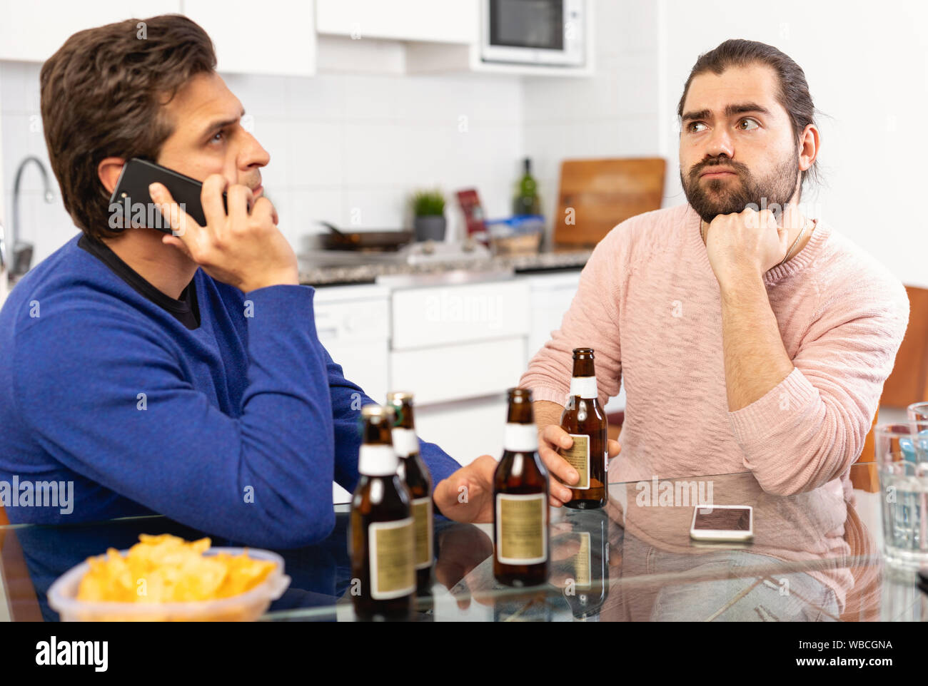 Two concerned men talking and laughing while enjoying beer at home ...