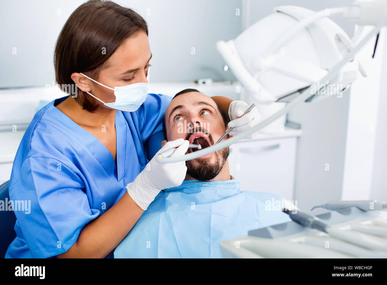 Pleasant stomatologist girl in uniform is taking visional inspection of ...
