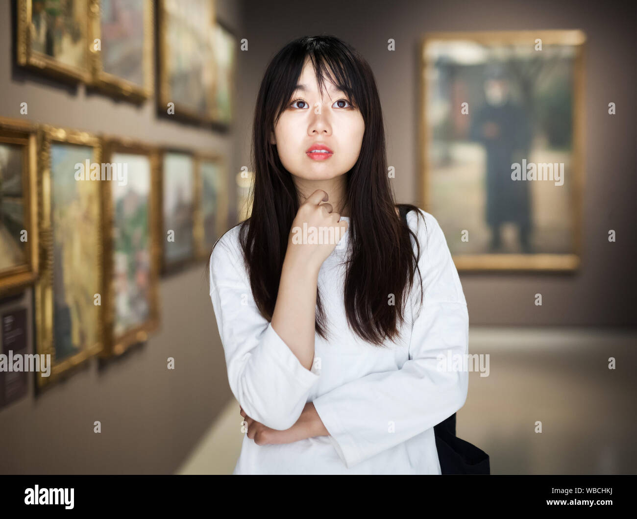 Portrait of intelligent chinese young woman near picture collection in ...
