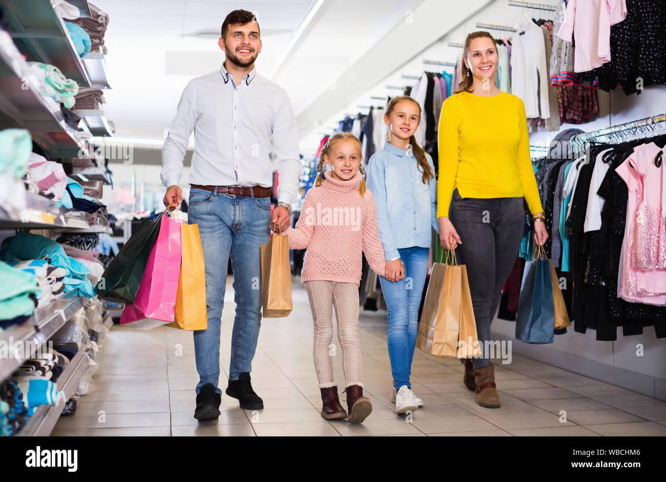 Young happy cheerful smiling parents with two little girls shopping in ...