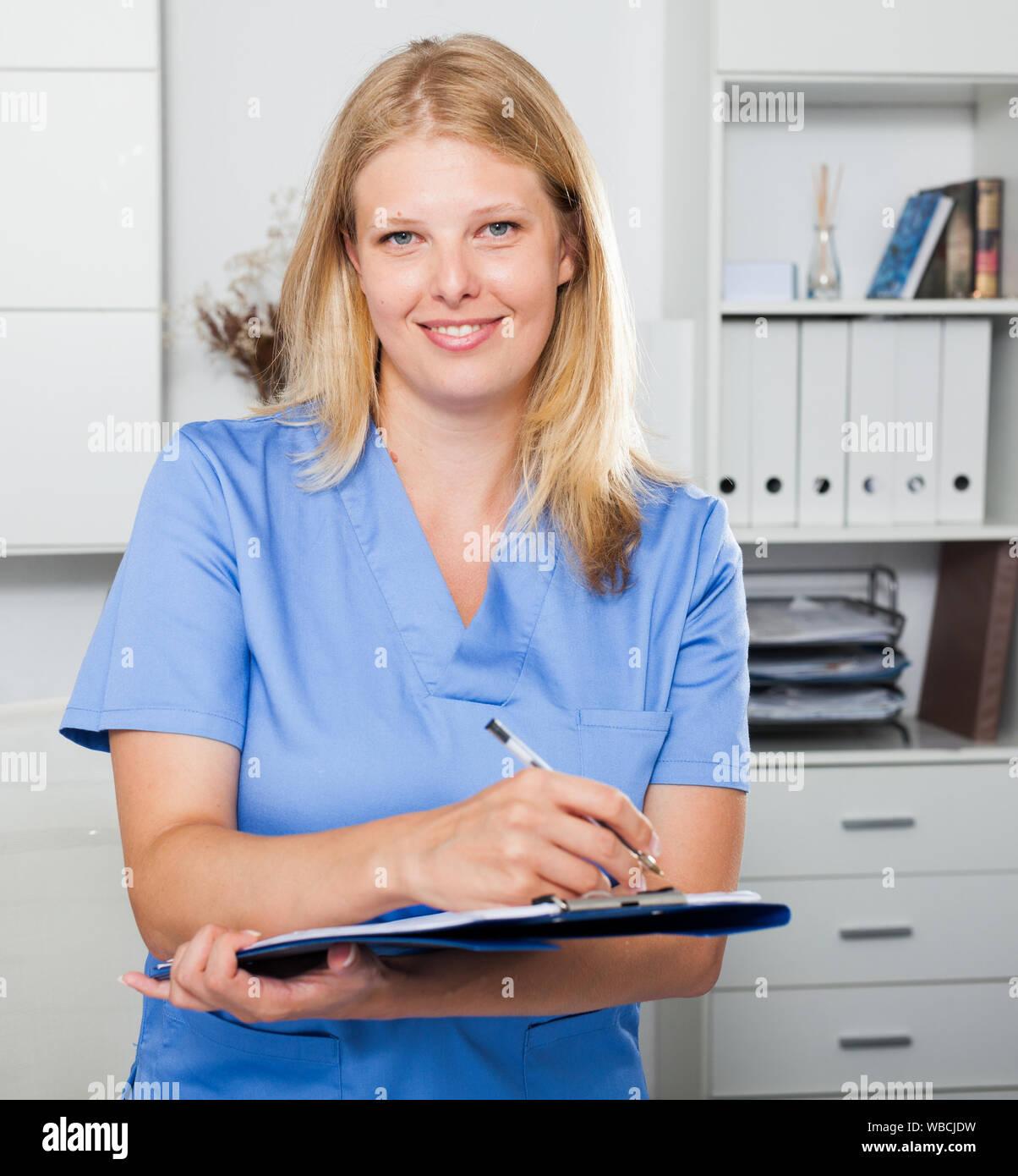 Smiling female nurse in formal wear registering information in form ...