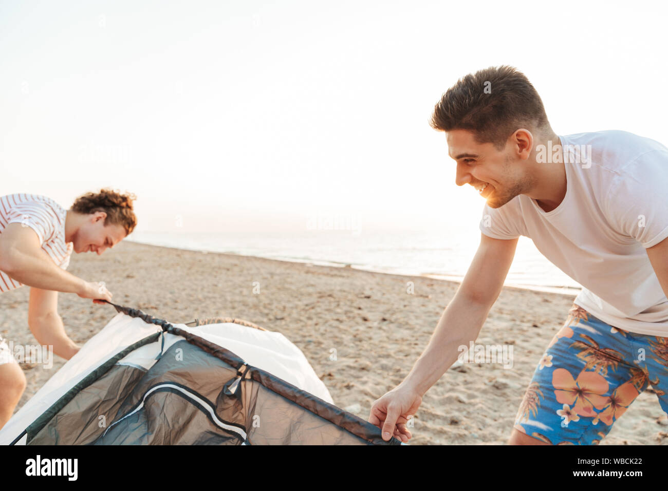 Two happy men building a tent at the beach for camping Stock Photo - Alamy