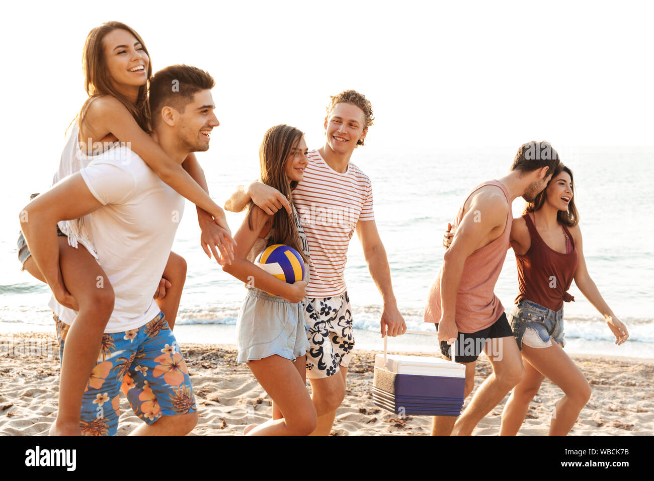 Back view of a group of friends walking at the beach, laughing ...