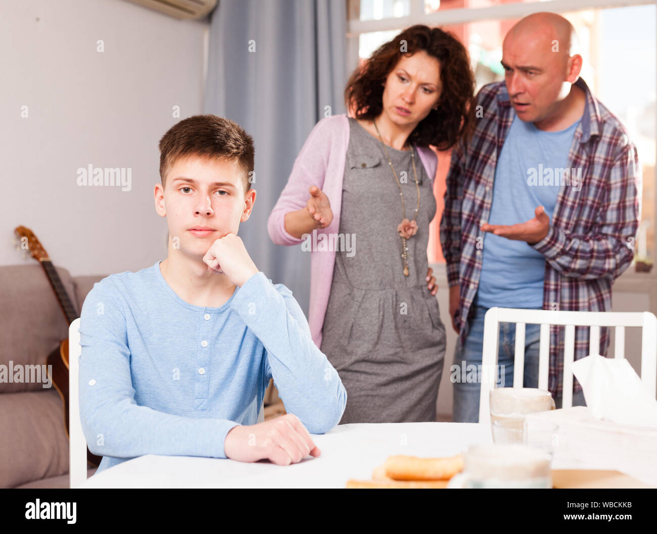 Portrait of upset teenage boy scolded by mother and father at home ...