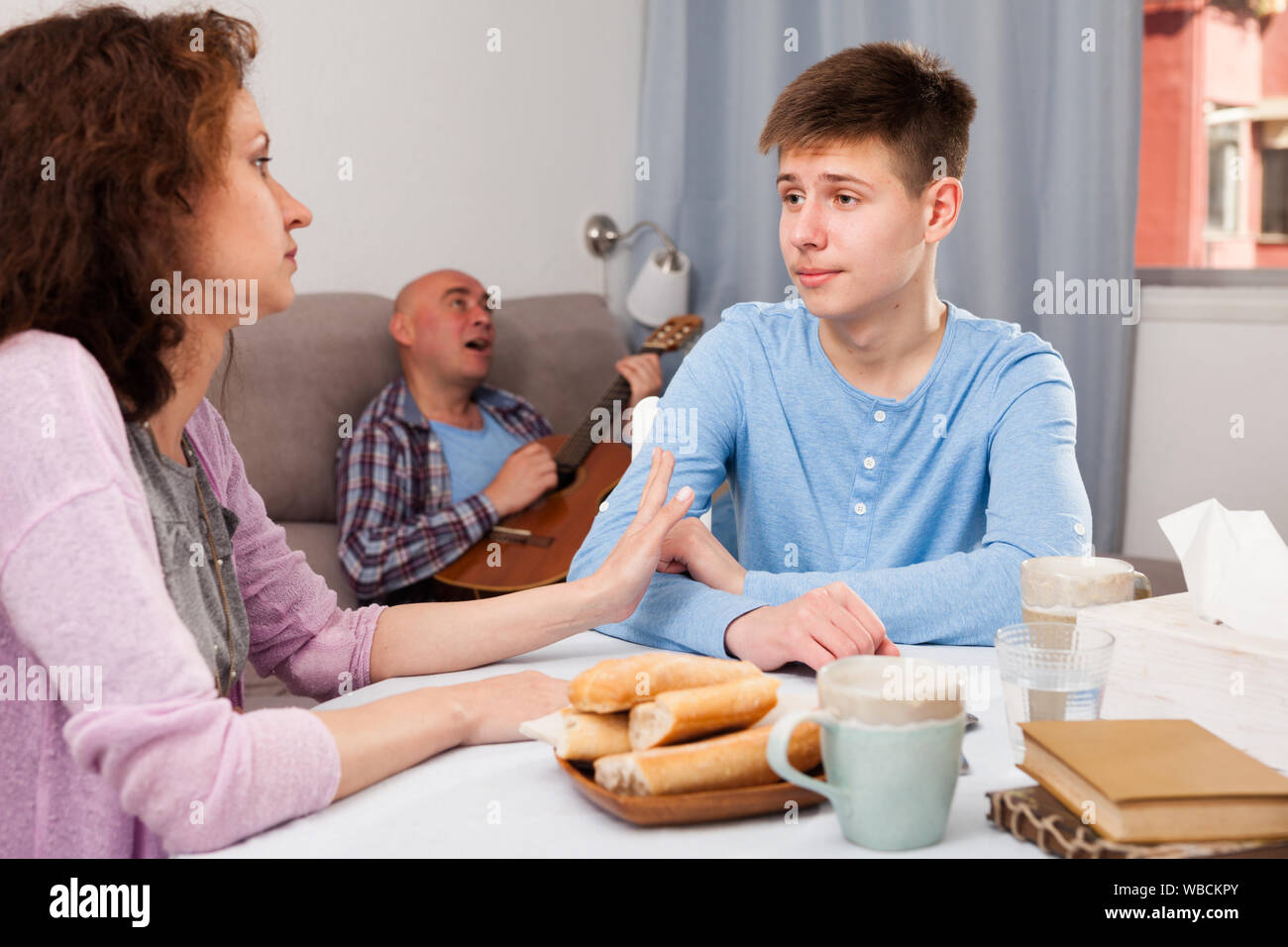 Focused teenager discussing serious topic with his mother while father ...