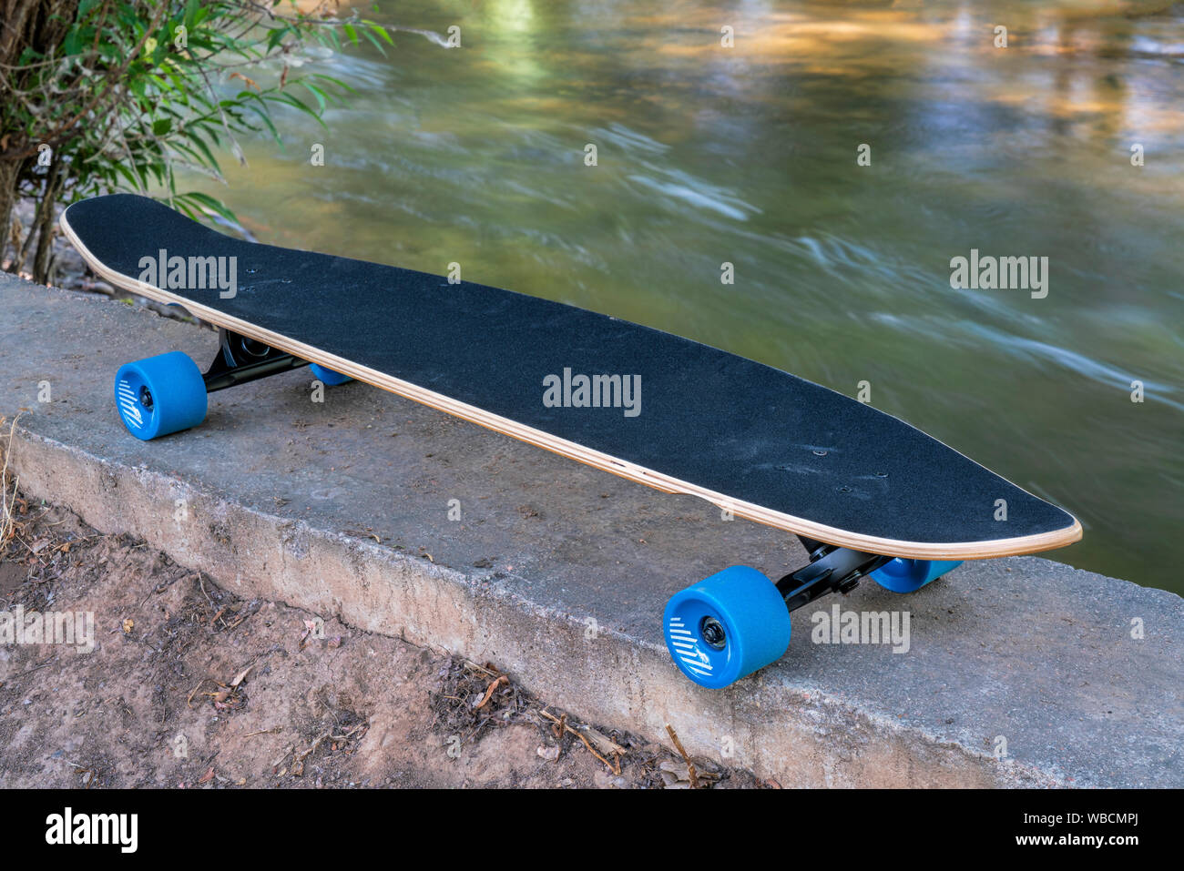cruising longboard with blue wheels on a river shore Stock Photo - Alamy