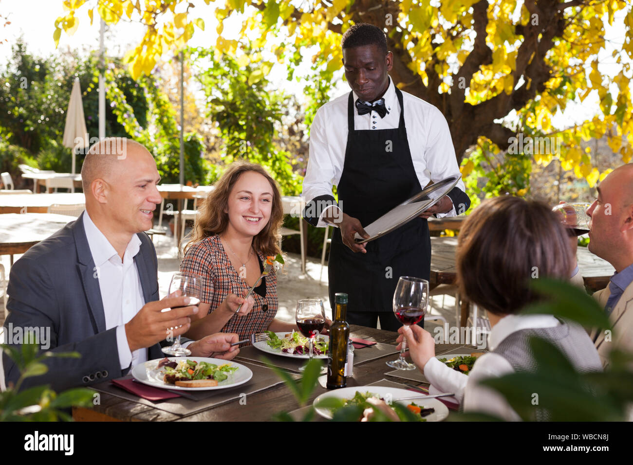 Waiter and four guests at open-air restaurant summer Stock Photo - Alamy