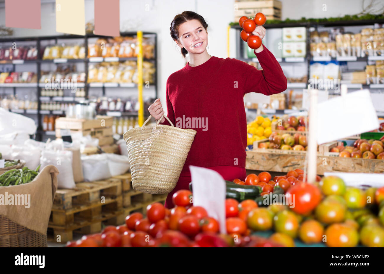 Portrait of smiling female customer selecting tomatoes in grocery store ...