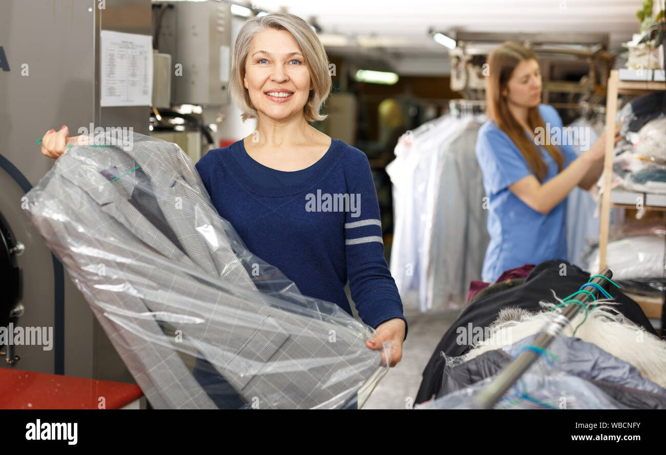Portrait of cheerful female laundry customer holding clean clothes on ...