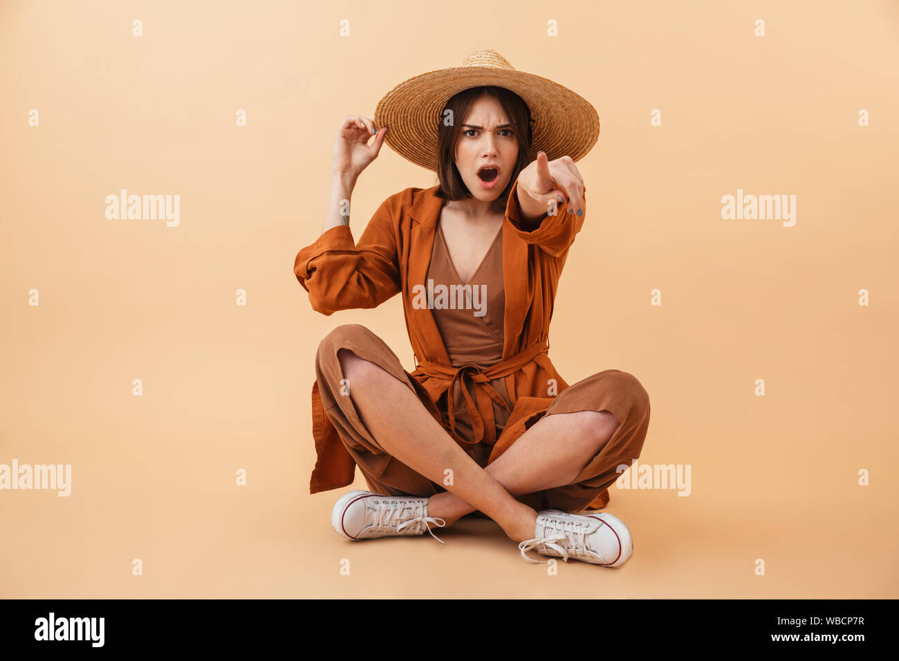 Beautiful angry young woman wearing straw hat and summer outfit sitting ...