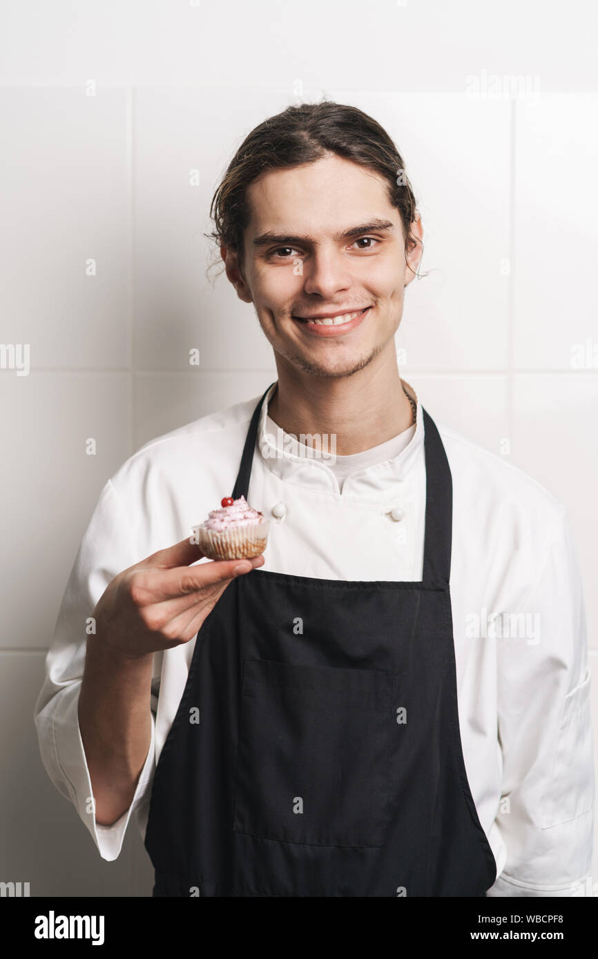 Image of a handsome young cook chef at the kitchen holding sweet cake ...