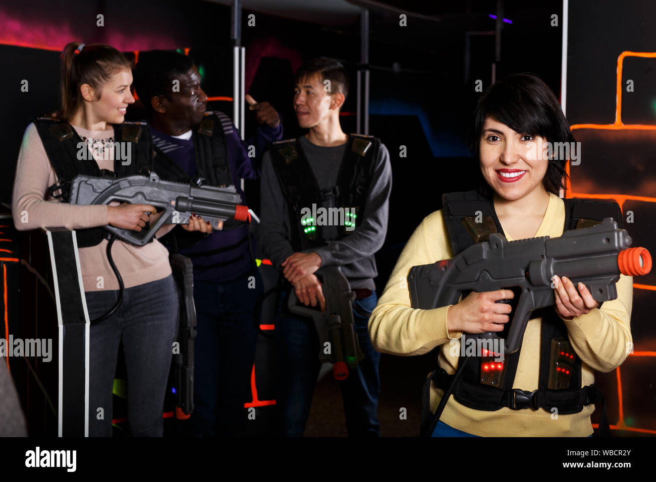 glad Latin woman lasertag player standing in full equipment before ...