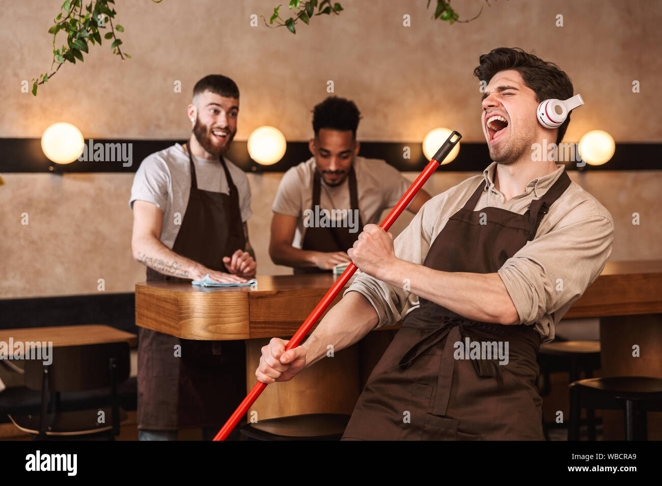 Three cheerful men baristas at the coffee shop, cleaning cafe after ...
