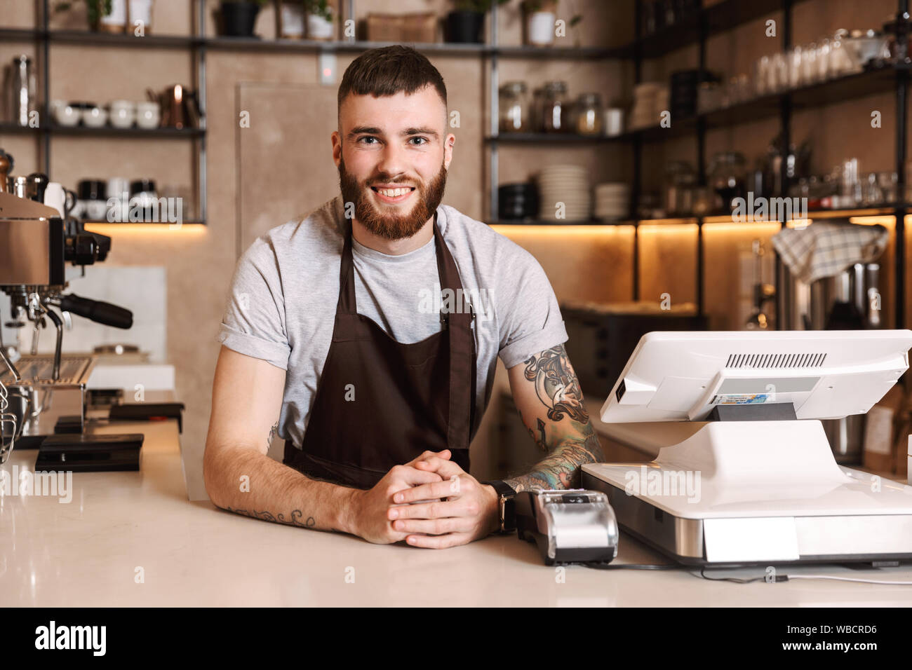 Smiling attractive man barista standing behind the counter at the ...