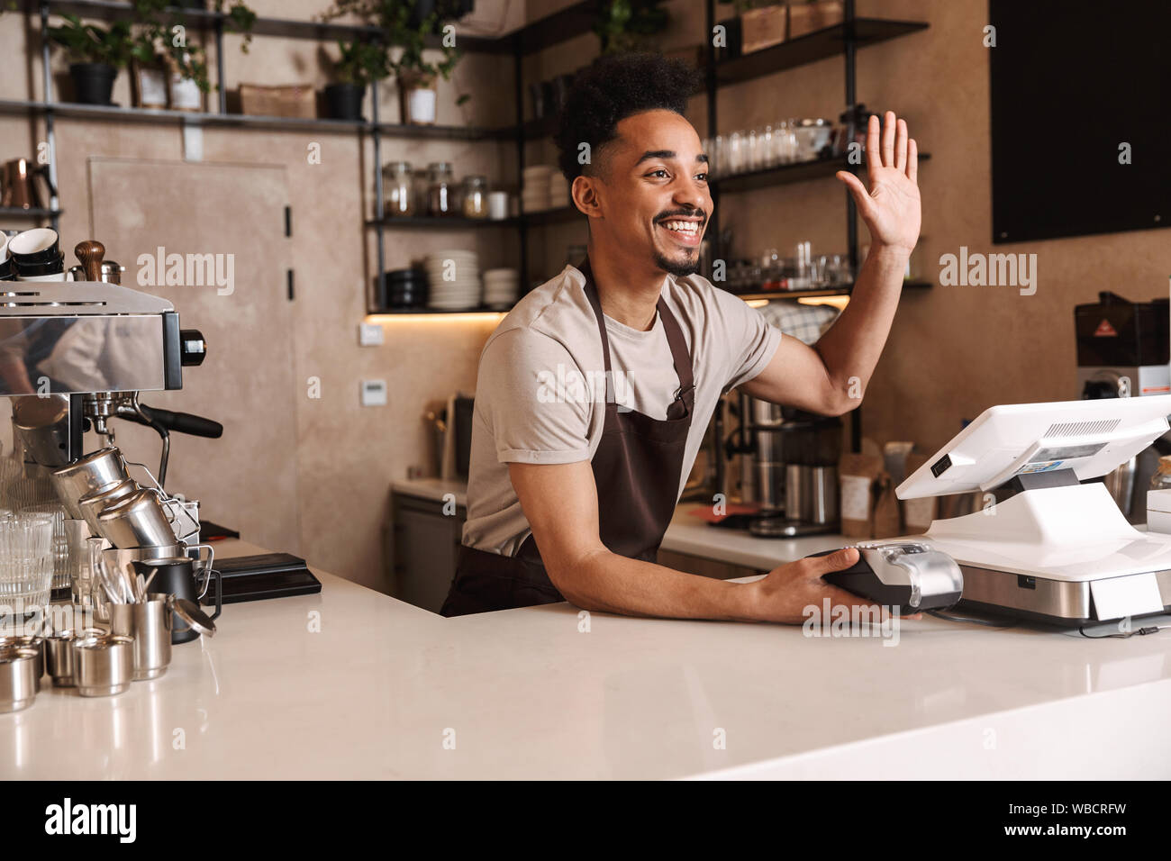 Smiling attractive african man barista standing behind the counter at ...