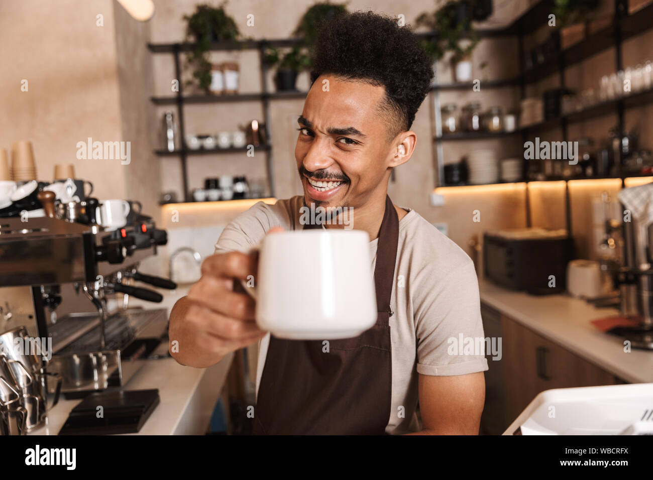 Smiling attractive african man barista standing behind the counter at ...