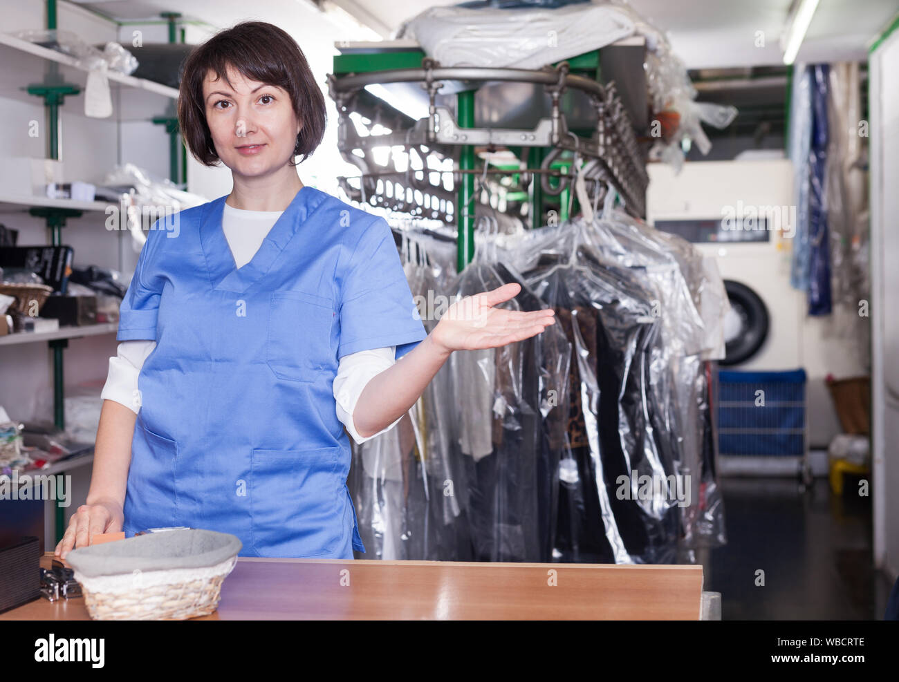 Polite female worker welcoming in modern dry cleaning salon standing at ...