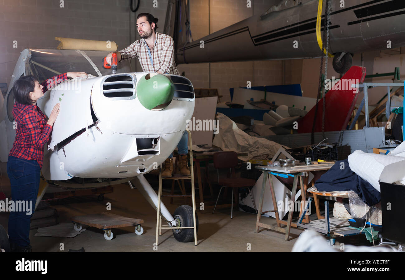 Female and male amateurs engaged in repairing old light plane in ...